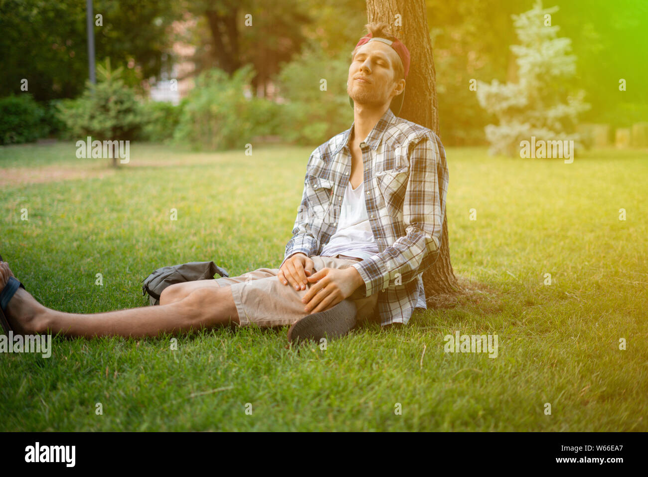 young male sleeping in the public park on the grass under the tree ...