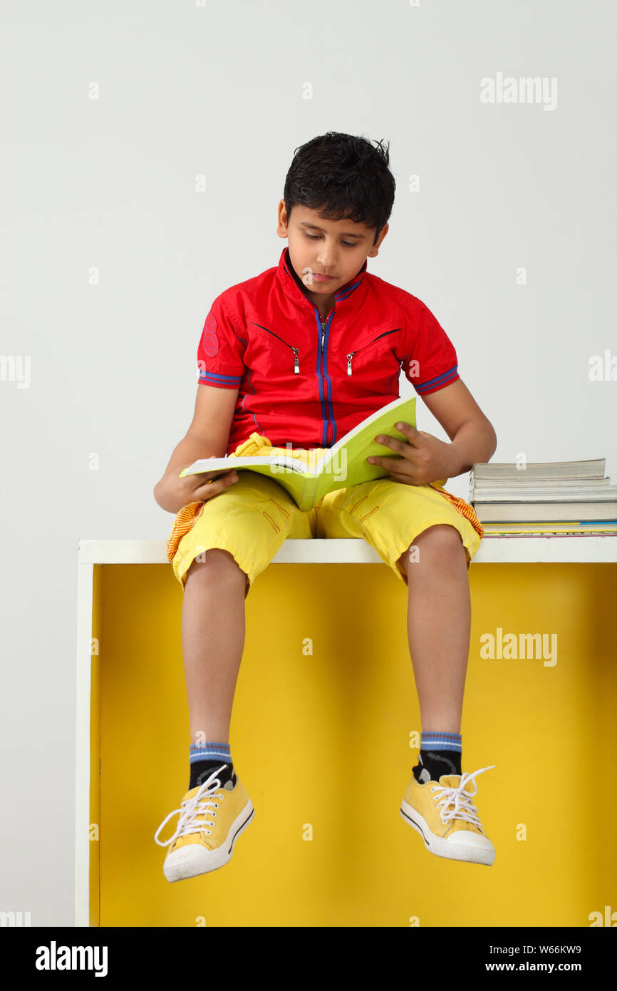 Boy sitting on desk and reading a book Stock Photo - Alamy