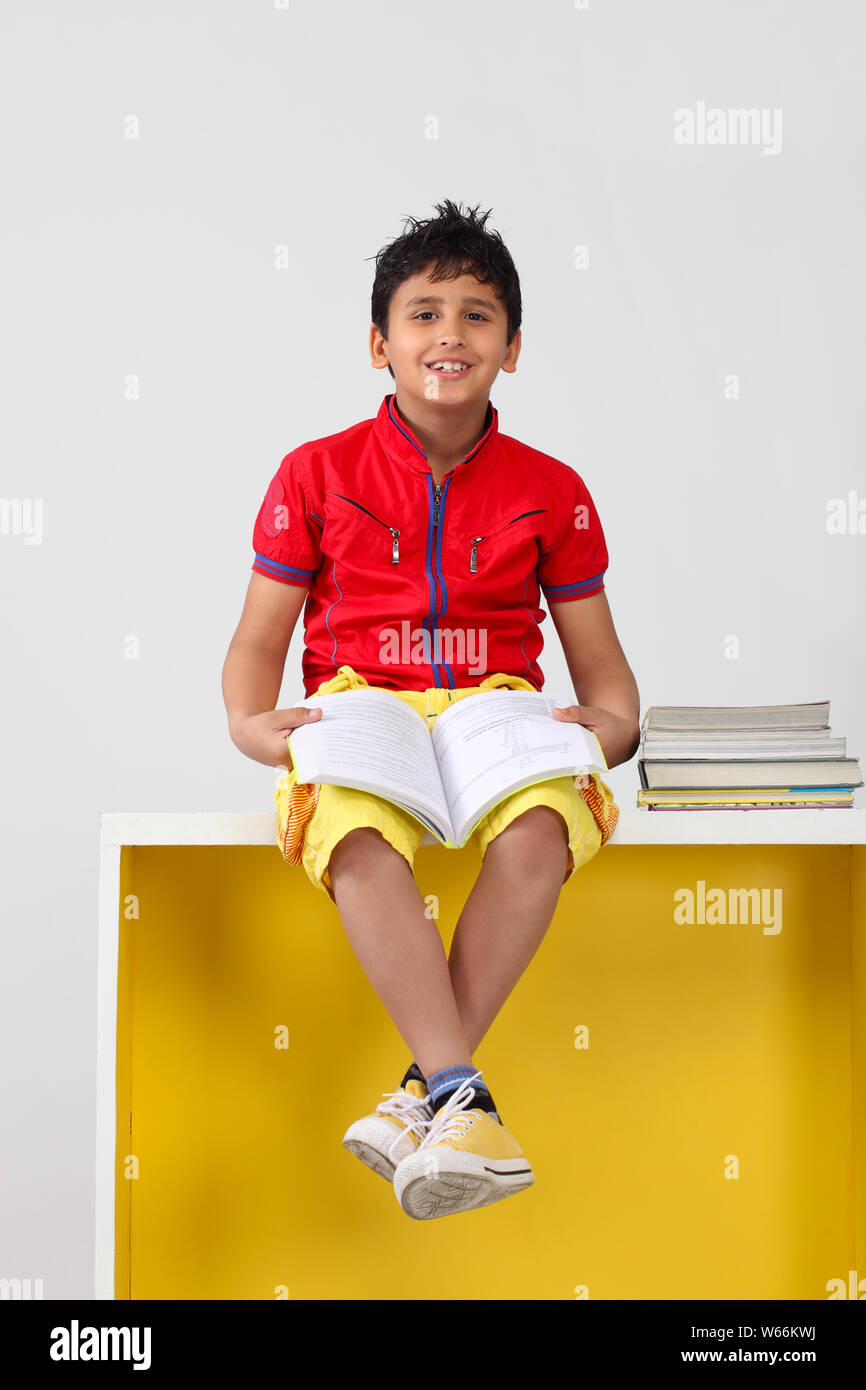 Boy sitting on desk and reading a book Stock Photo - Alamy