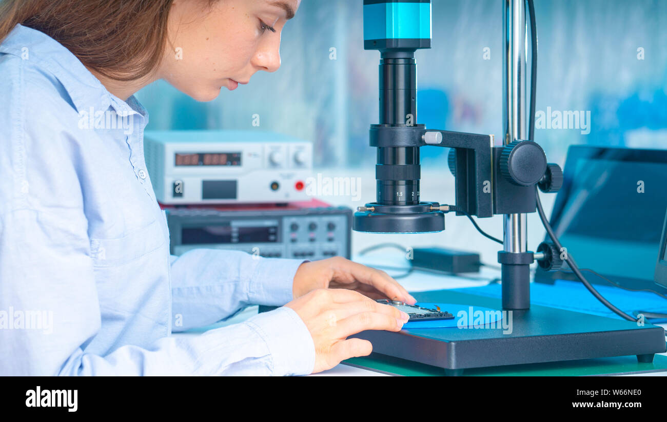 Young woman in inspection electronics PCB devise. Modern electronics ...