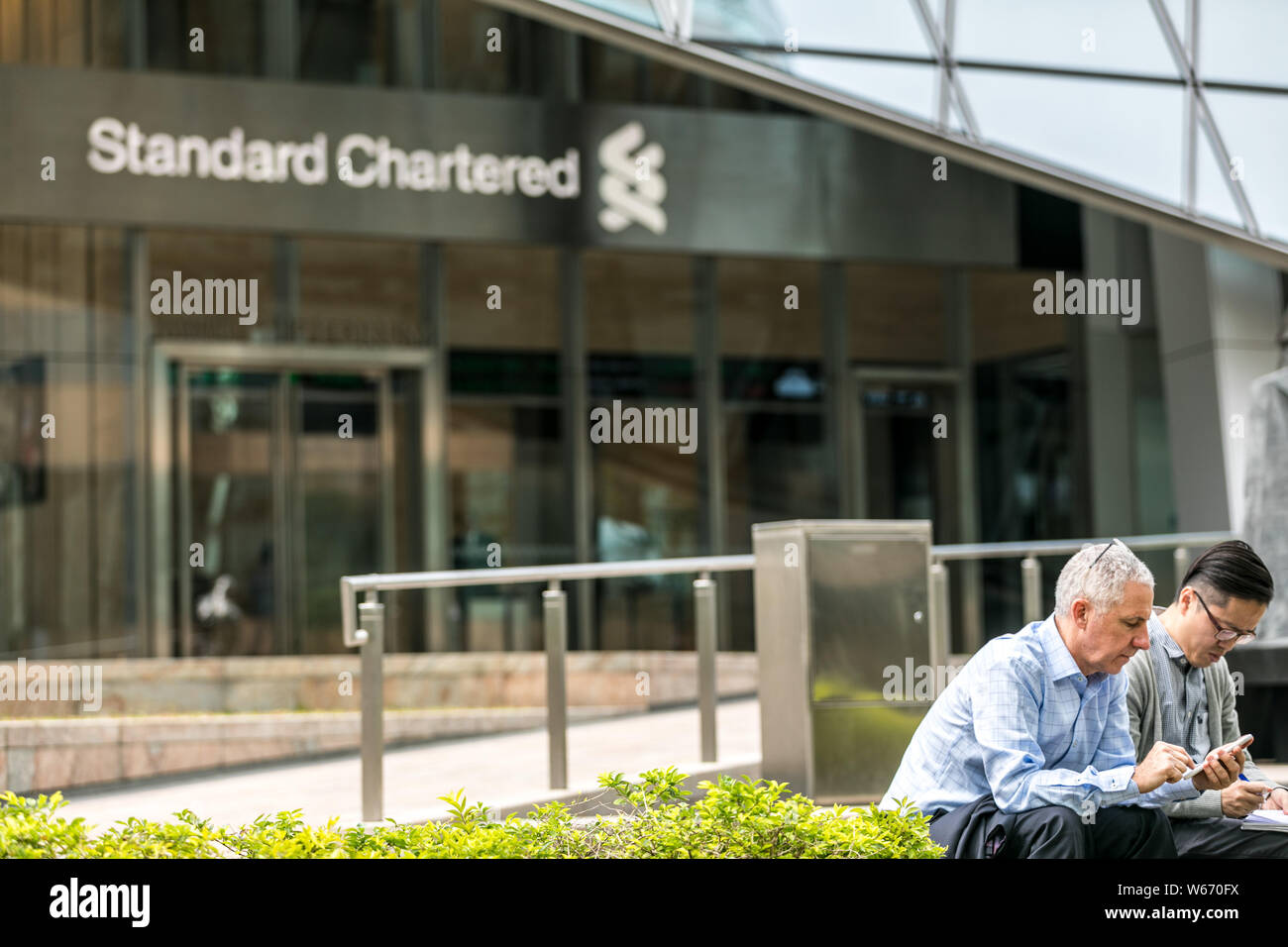 --FILE--People sit near a branch of London-listed Standard Chartered ...