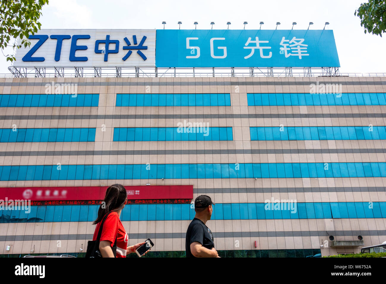 --FILE--Pedestrians walk past a signboard of ZTE on the rooftop of an ...