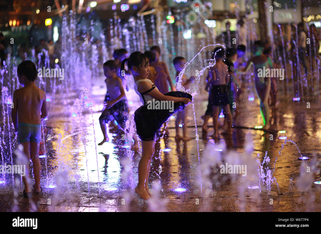 Young Chinese kids play with water to cool off in a fountain in front ...