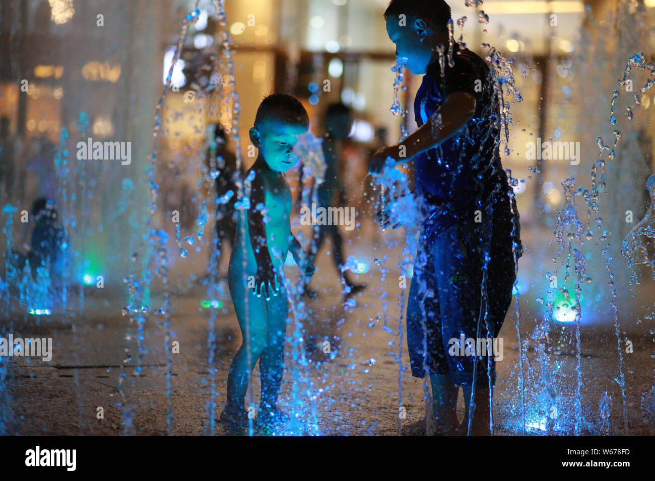 Young Chinese kids play with water to cool off in a fountain in front ...