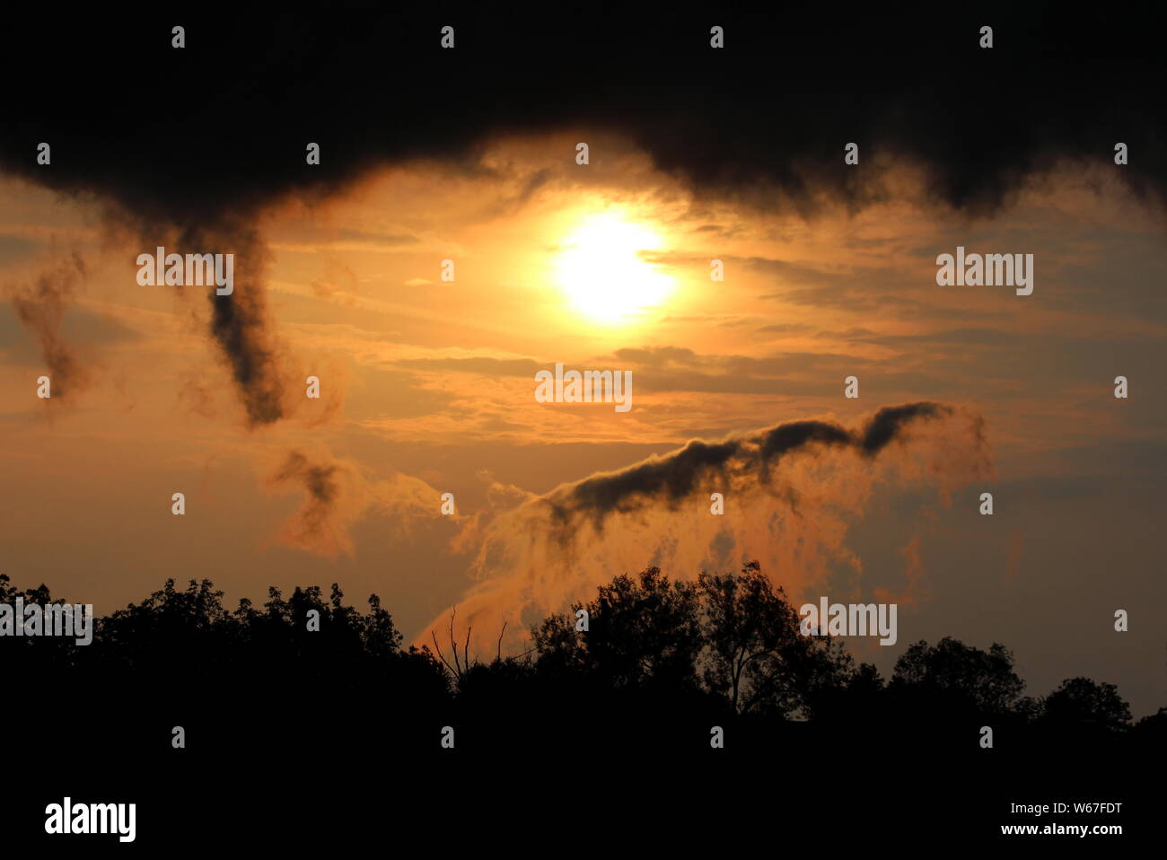 Dramatic stormy clouds surrounding sun at sunset over local forest on ...