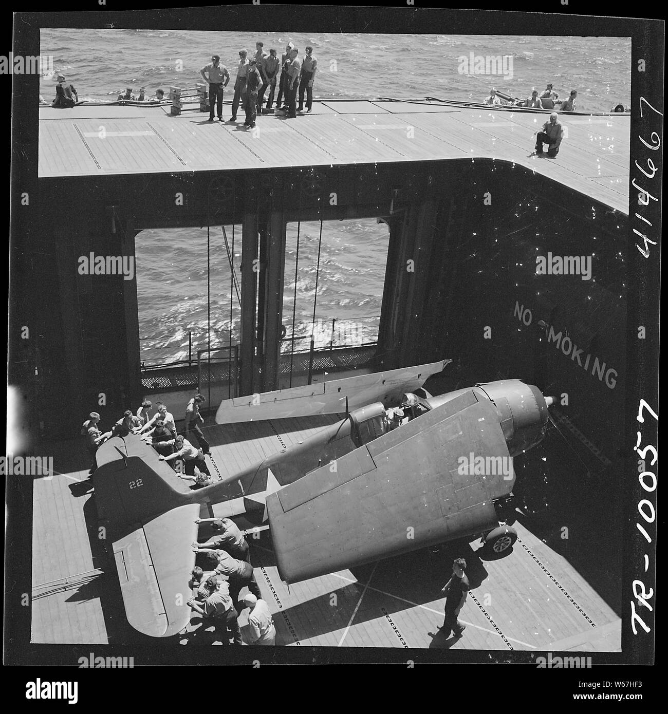 Navy crewmen aboard the USS Monterey (CVL-26) bringing an F6F to the ...