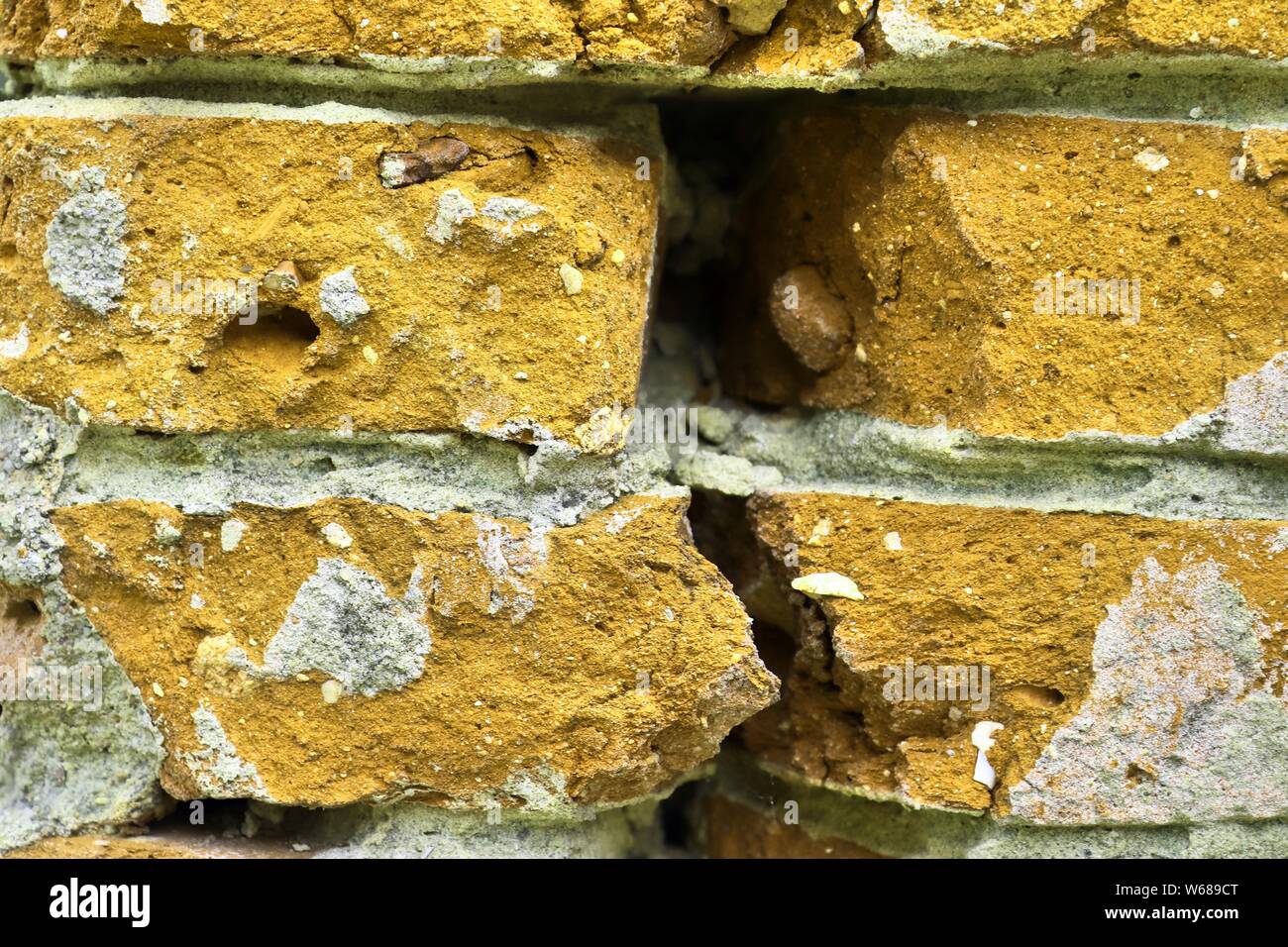 Yellow brick walls with old and weathered stones and cracks im high ...