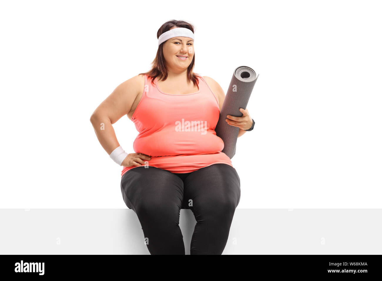 Plus size young female with an exercise mat sitting on a panel isolated ...