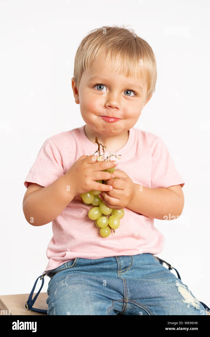Baby boy eating grapes and smiling in the studio isolated on white ...
