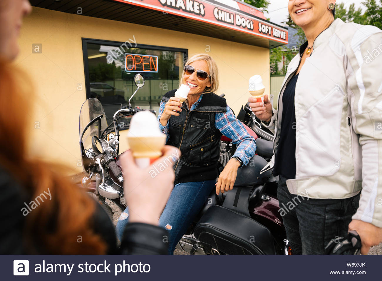 Women friends eating ice cream on motorcycles in parking lot of drive ...