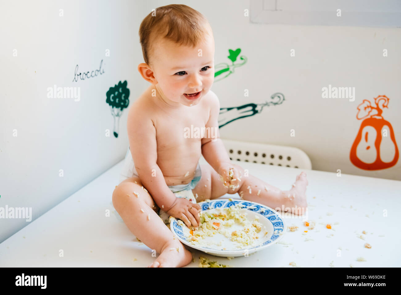 Baby smiling while testing his first solid food by himself, alternative ...