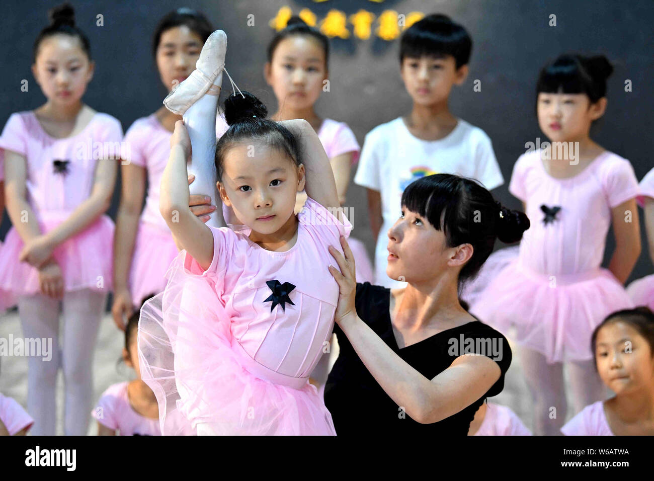 A Chinese Teacher Helps A Young Girl Stretch Her Leg To Learn Dancing