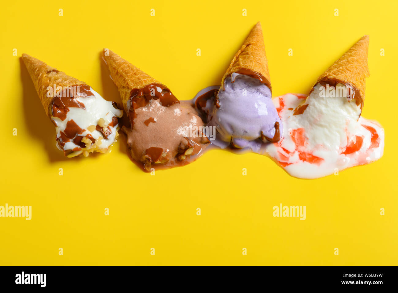 side view multiple flavor ice cream cones melted on yellow background ...