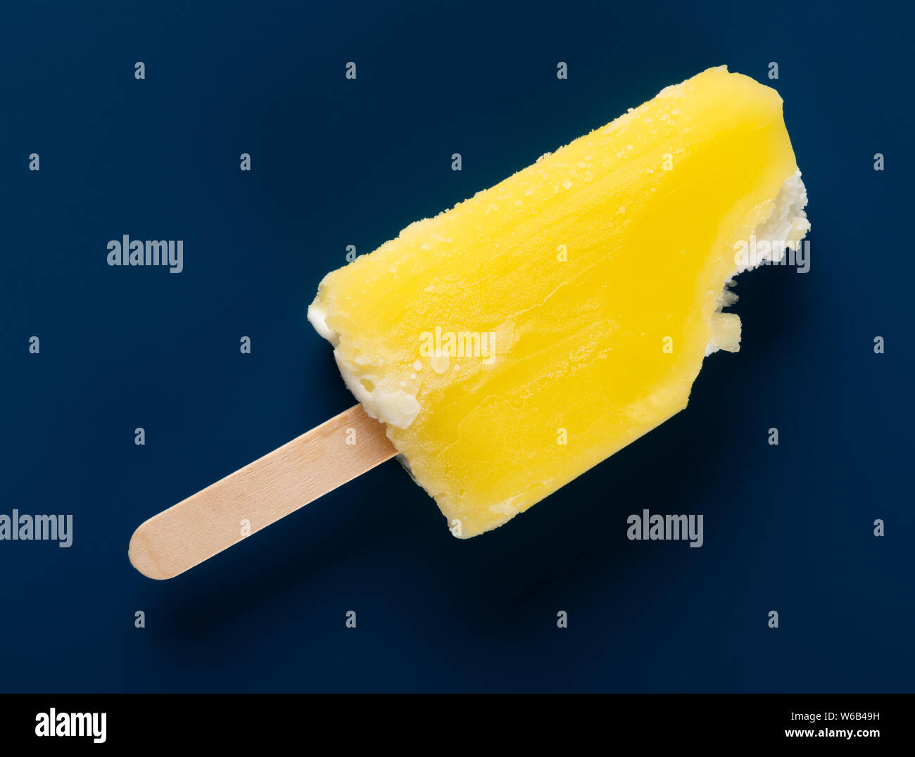 yellow popsicle with some bites on a dark blue background Stock Photo ...