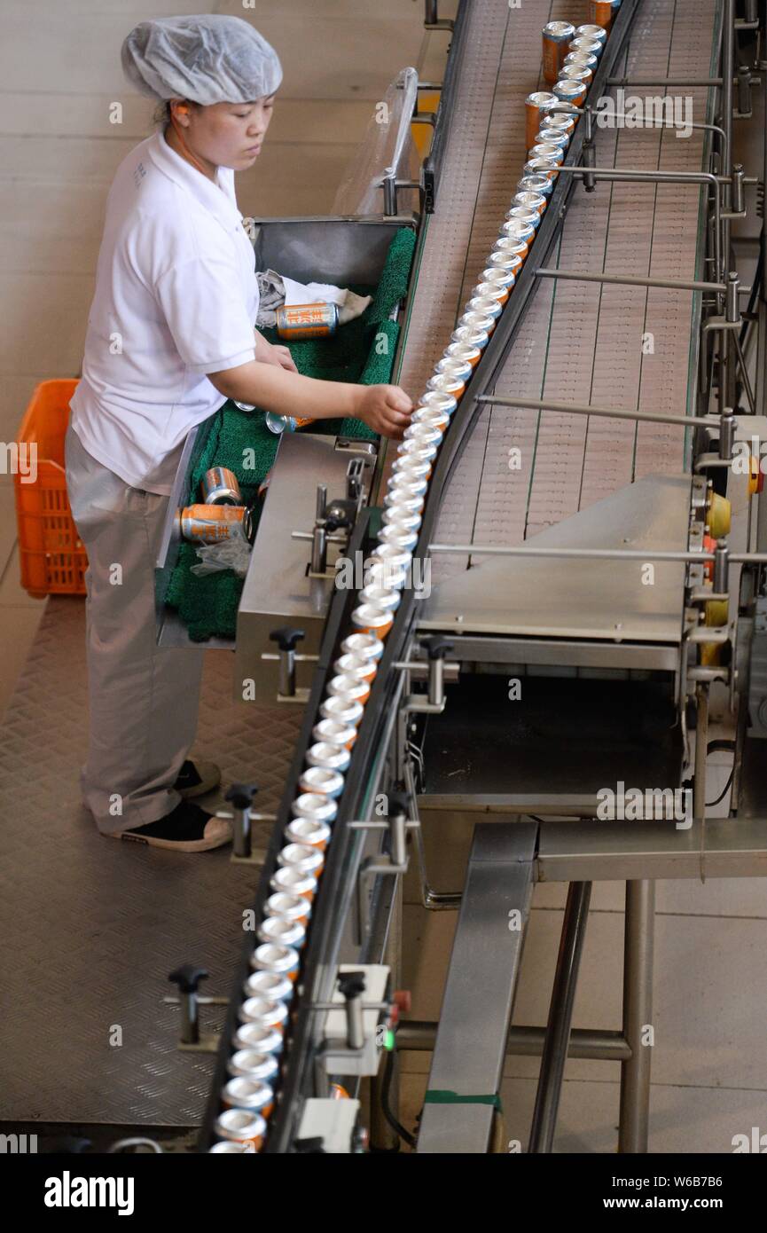 A Chinese worker checks the production of cans of orange soda on the ...