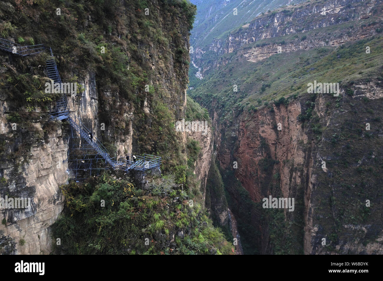 People climb the steel ladder on the cliff in a mountainous area in ...