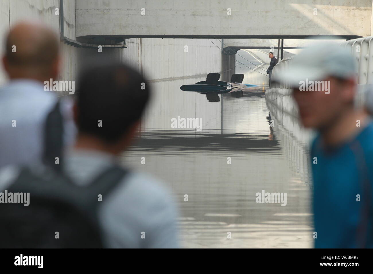 Local residents watch a submerged bus stuck under a flooded bridge ...