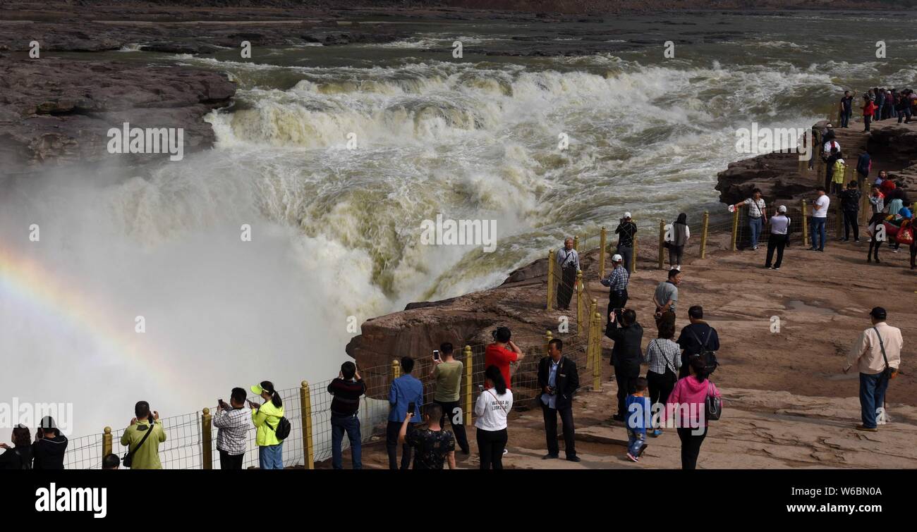 Tourists visit the Hukou Waterfall scenic spot as a rainbow arches over ...