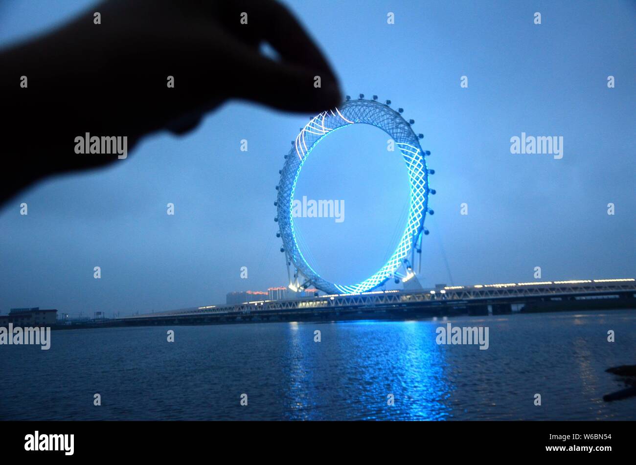 A local resident poses for a creative photo with a "big ring", Bailang River Bridge Ferris Wheel ...