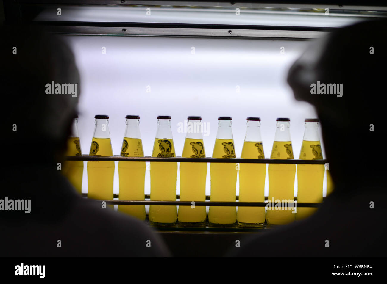 Chinese workers monitor the production of bottles of orange soda on the ...
