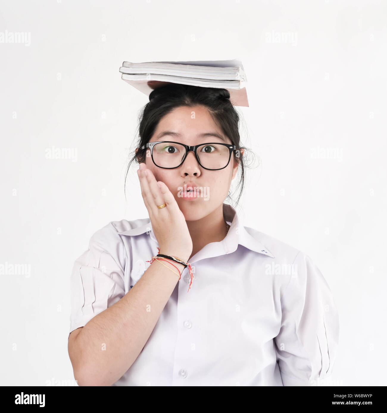 Happy Asian student in uniform putting books stack on her head ...
