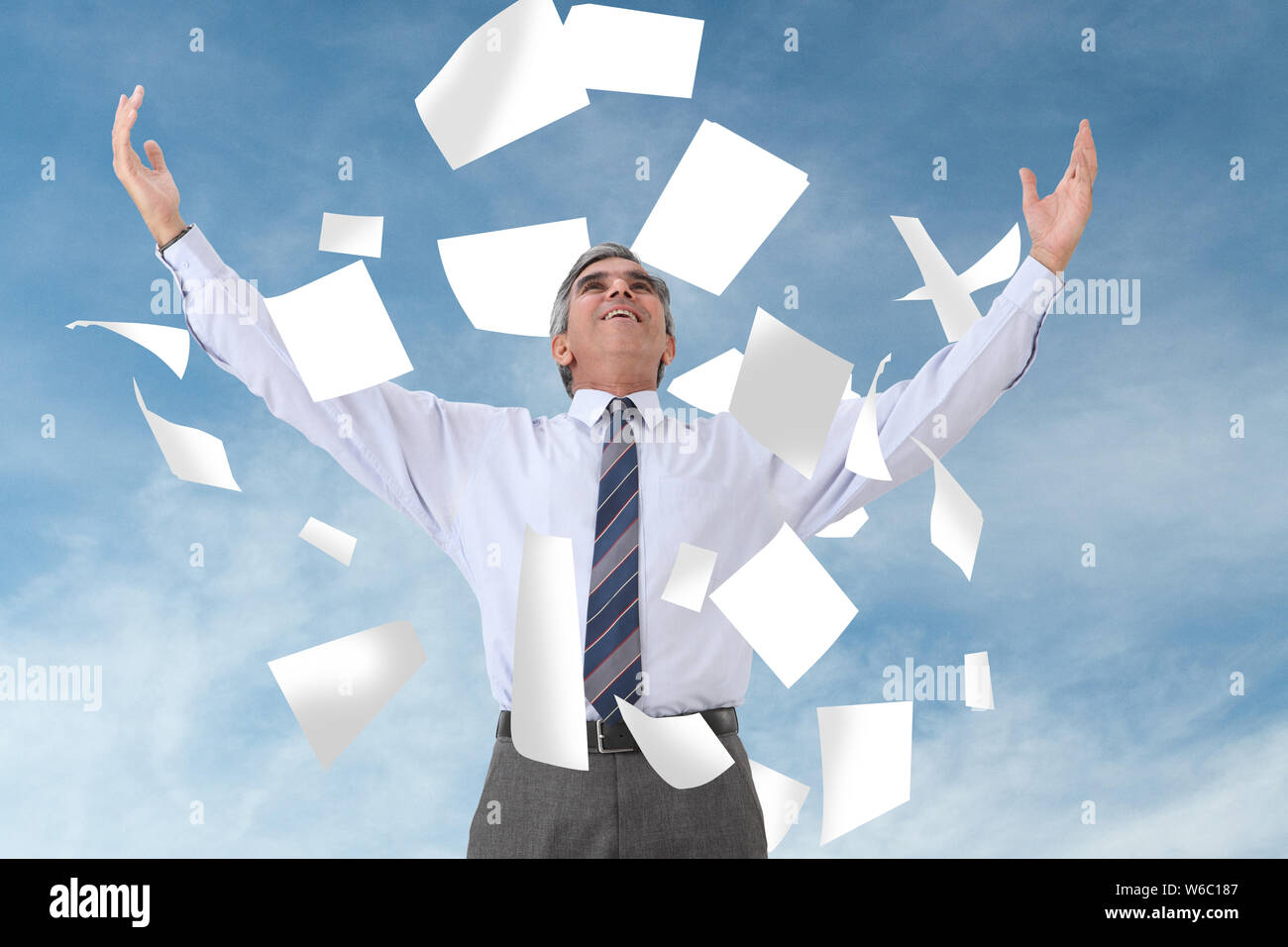 Papers falling on a businessman standing with his arms outstretched ...