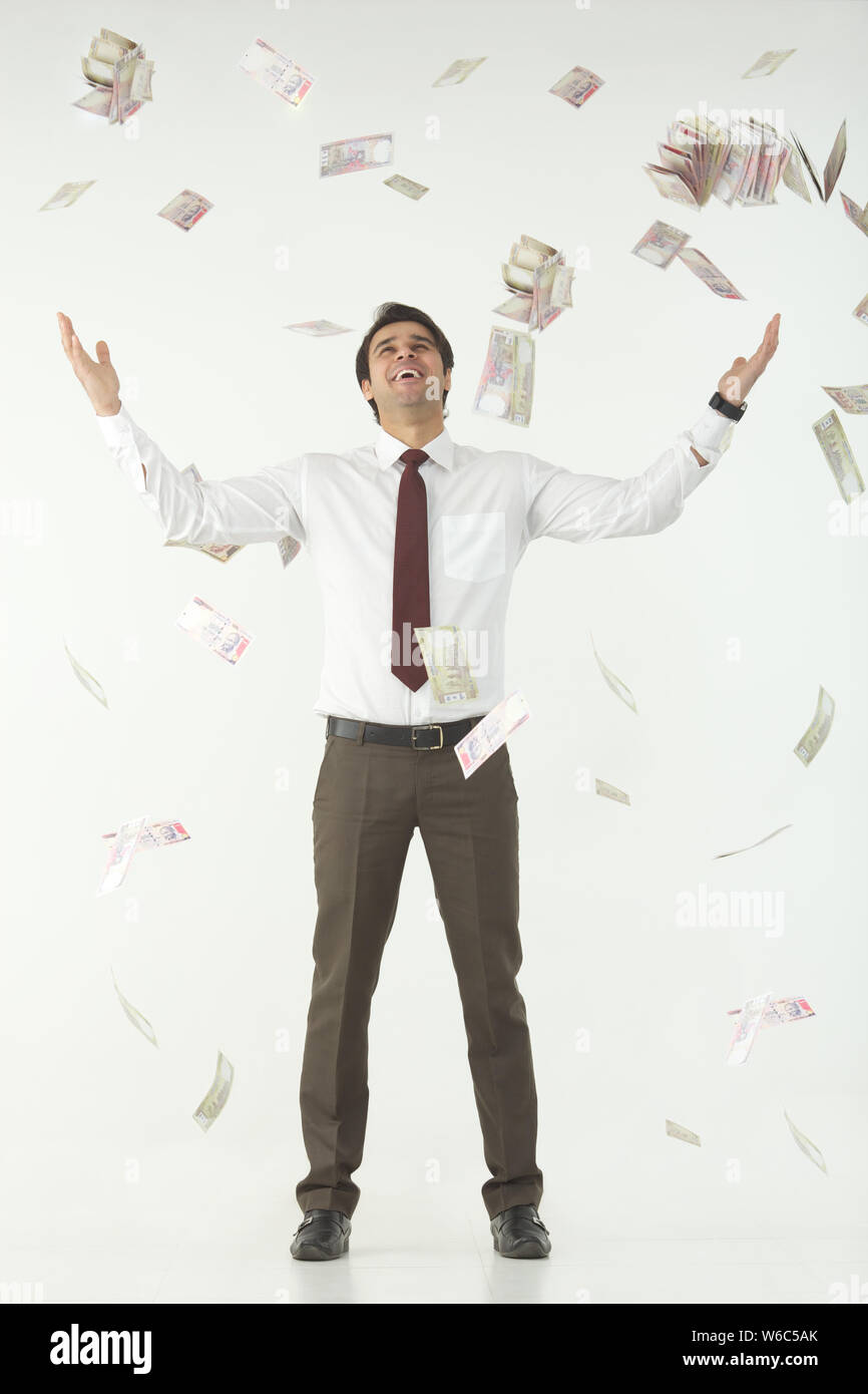 Money falling on a businessman standing with his arms outstretched ...