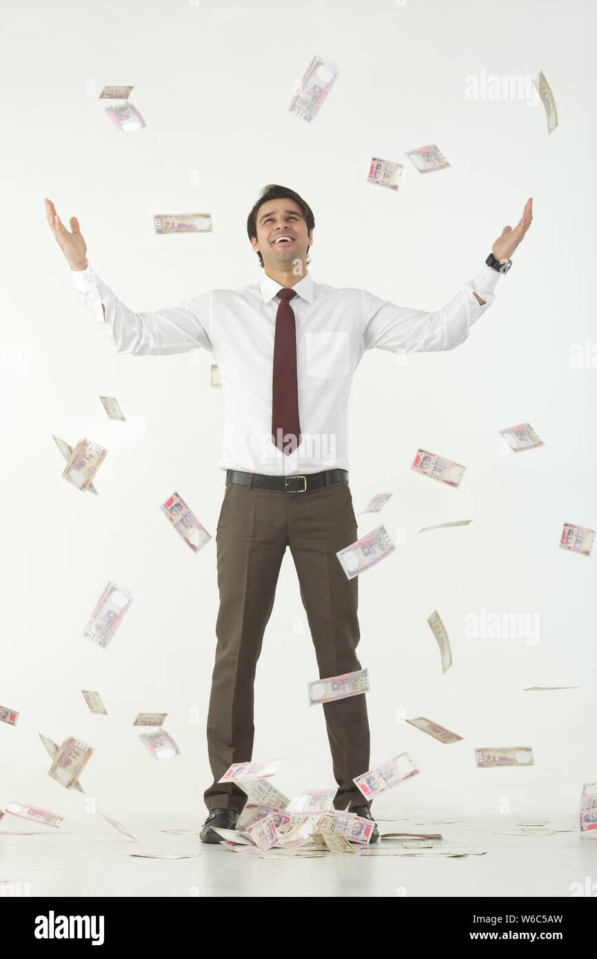 Money falling on a businessman standing with his arms outstretched ...