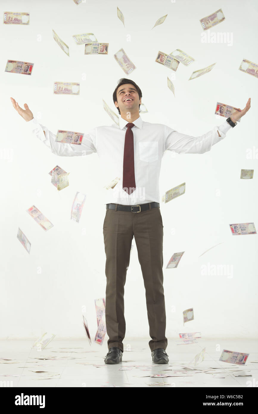 Money falling on a businessman standing with his arms outstretched ...