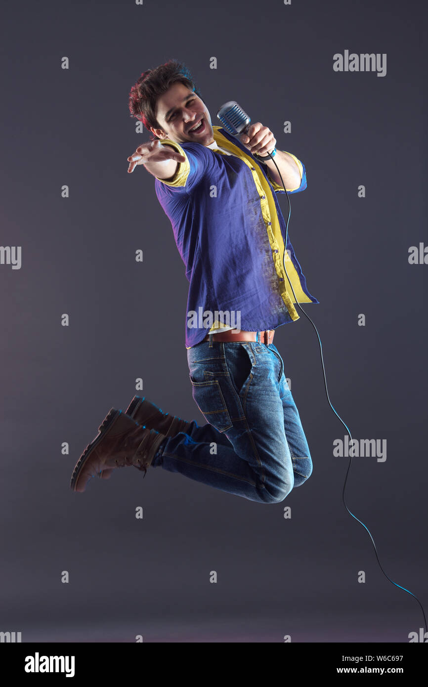 Man jumping in air singing into microphone Stock Photo - Alamy