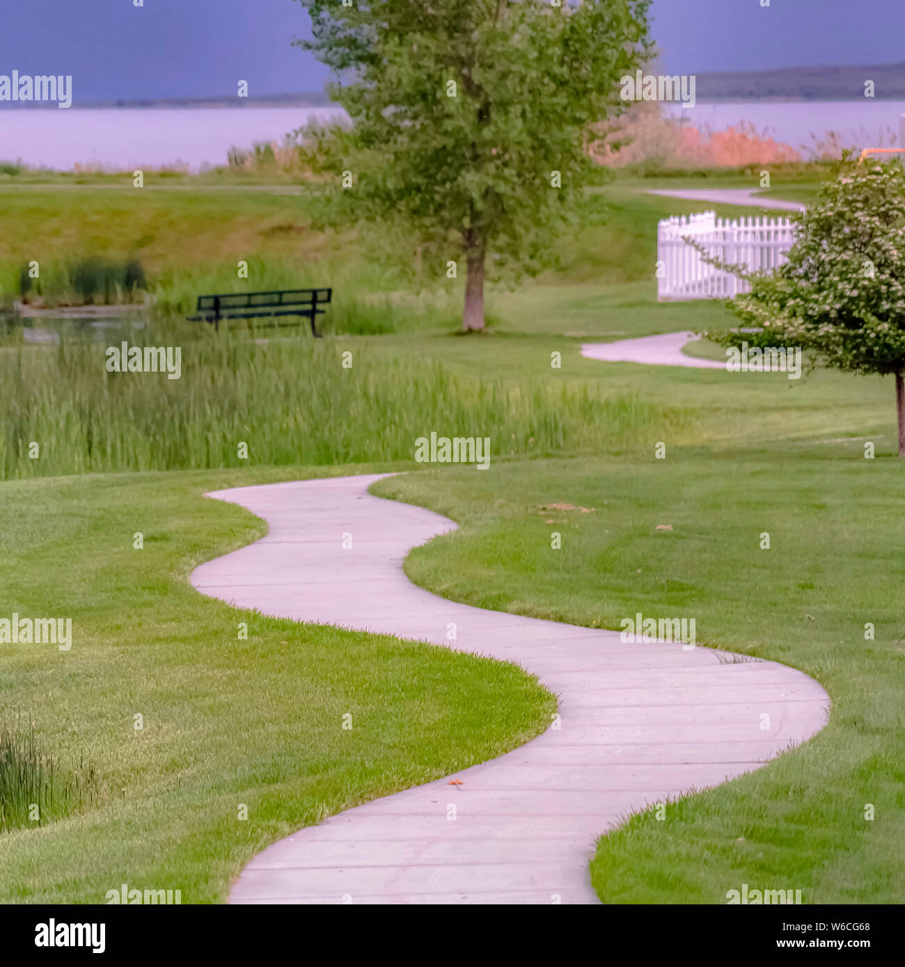 Square Pathway curving through grassy terrain with a pond and bench in ...