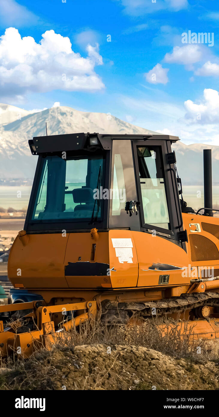 Vertical frame Yellow loader on a hill overlooking houses on a ...
