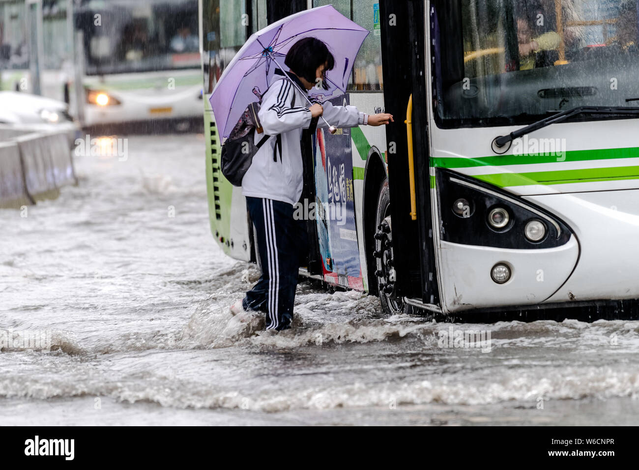 A student shields herself with an umbrella as she prepares to get on a ...