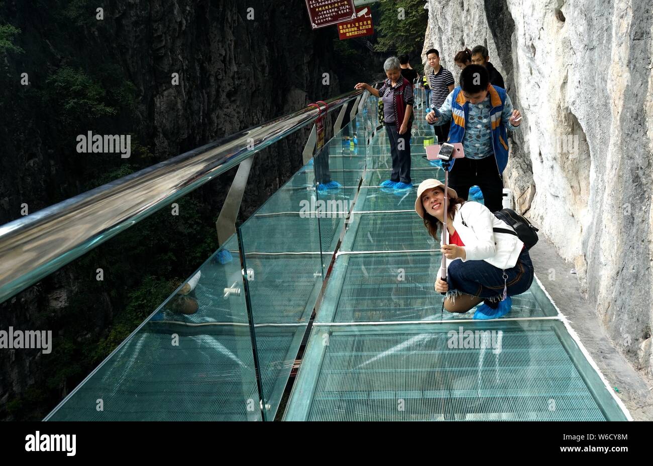 Tourists pose for photos on a glass walkway along the edge of a cliff ...