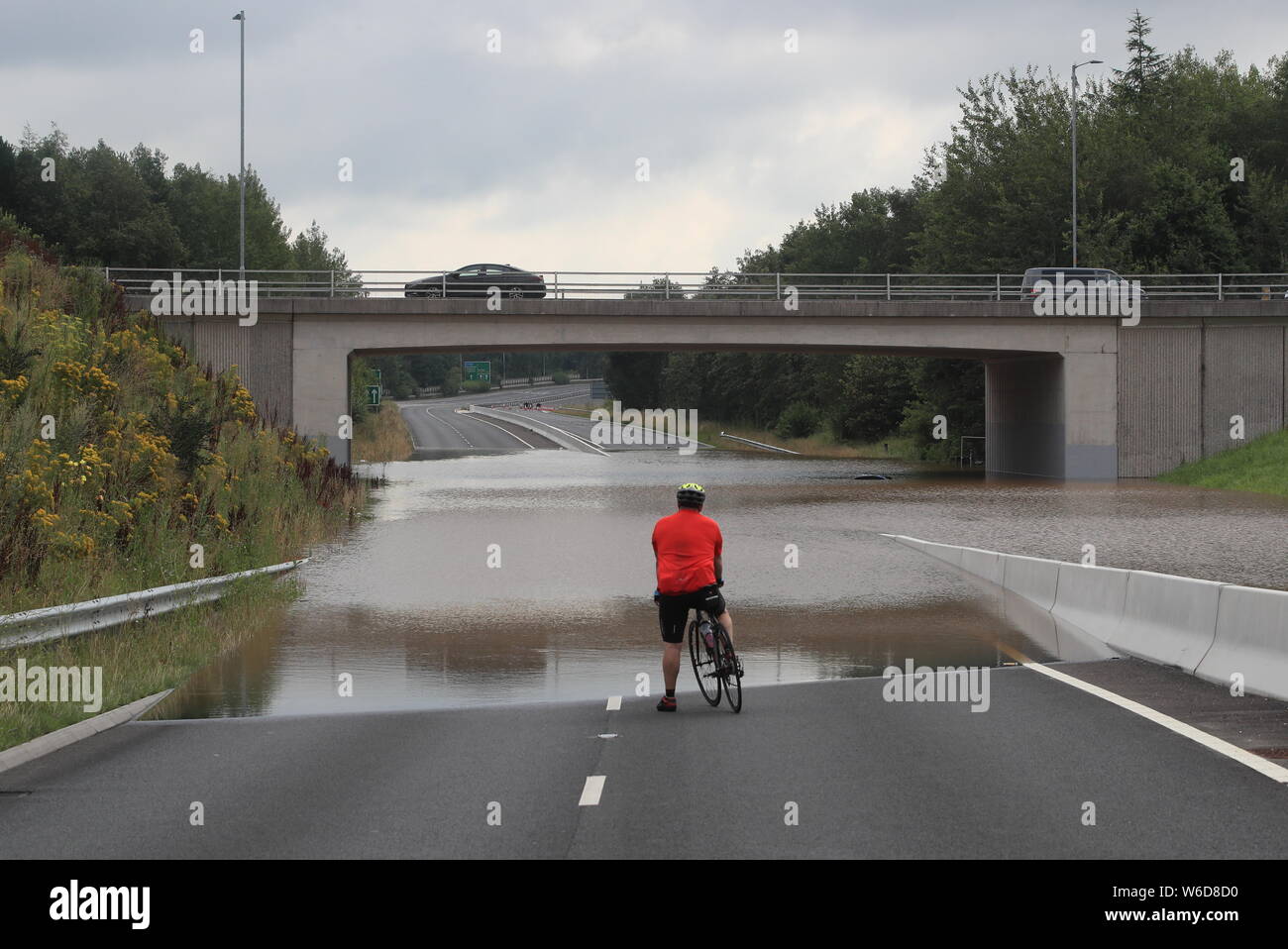 A bike rider comes to a halt as flood water blocks a road on the A555 ...