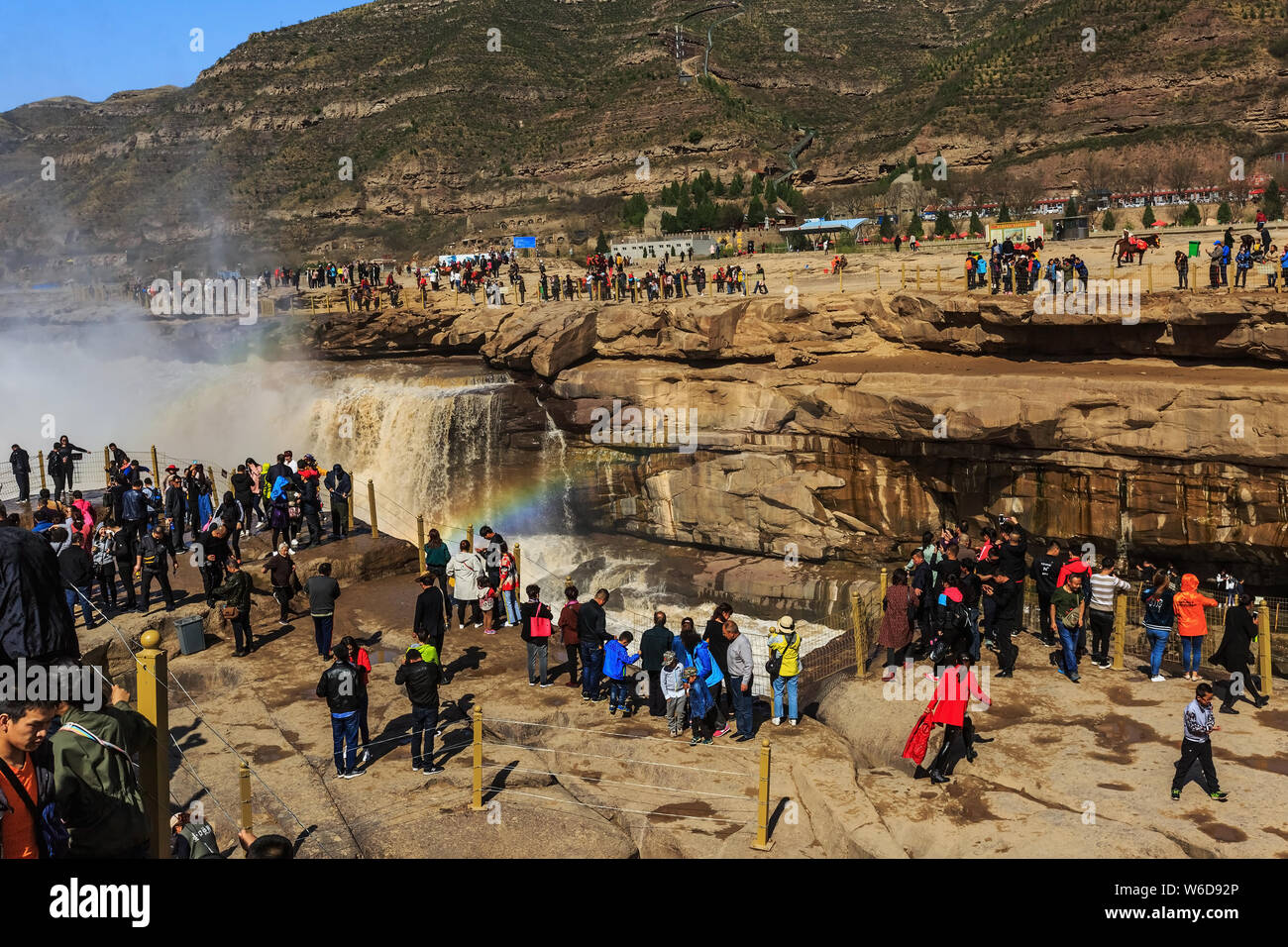 Tourists visit the Hukou Waterfall scenic spot as a rainbow arches over ...