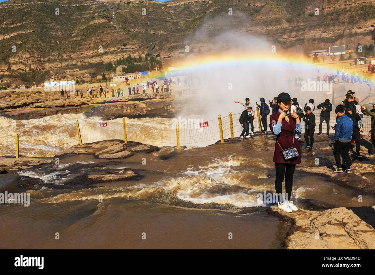 Tourists visit the Hukou Waterfall scenic spot as a rainbow arches over ...