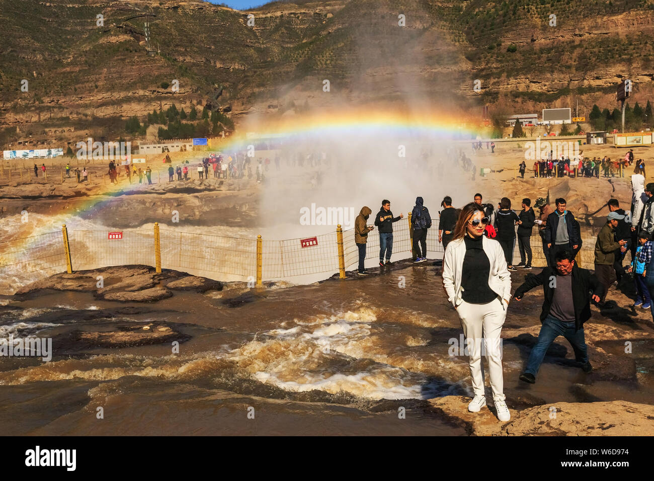 Tourists visit the Hukou Waterfall scenic spot as a rainbow arches over ...