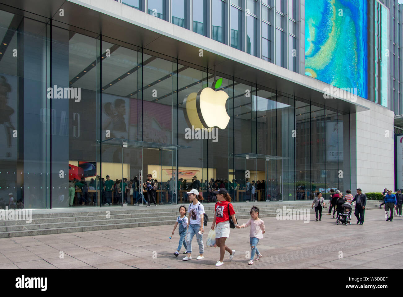 Pedestrians walk past an Apple Store with the leaf of the logo of Apple ...
