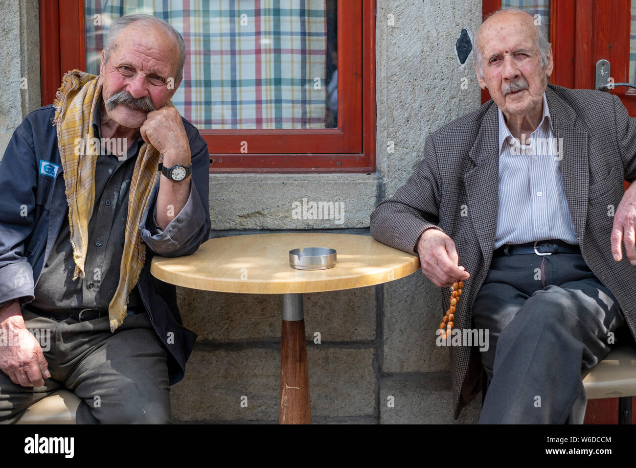 Two elderly Greek men sit in the shade of a village cafe observing the ...