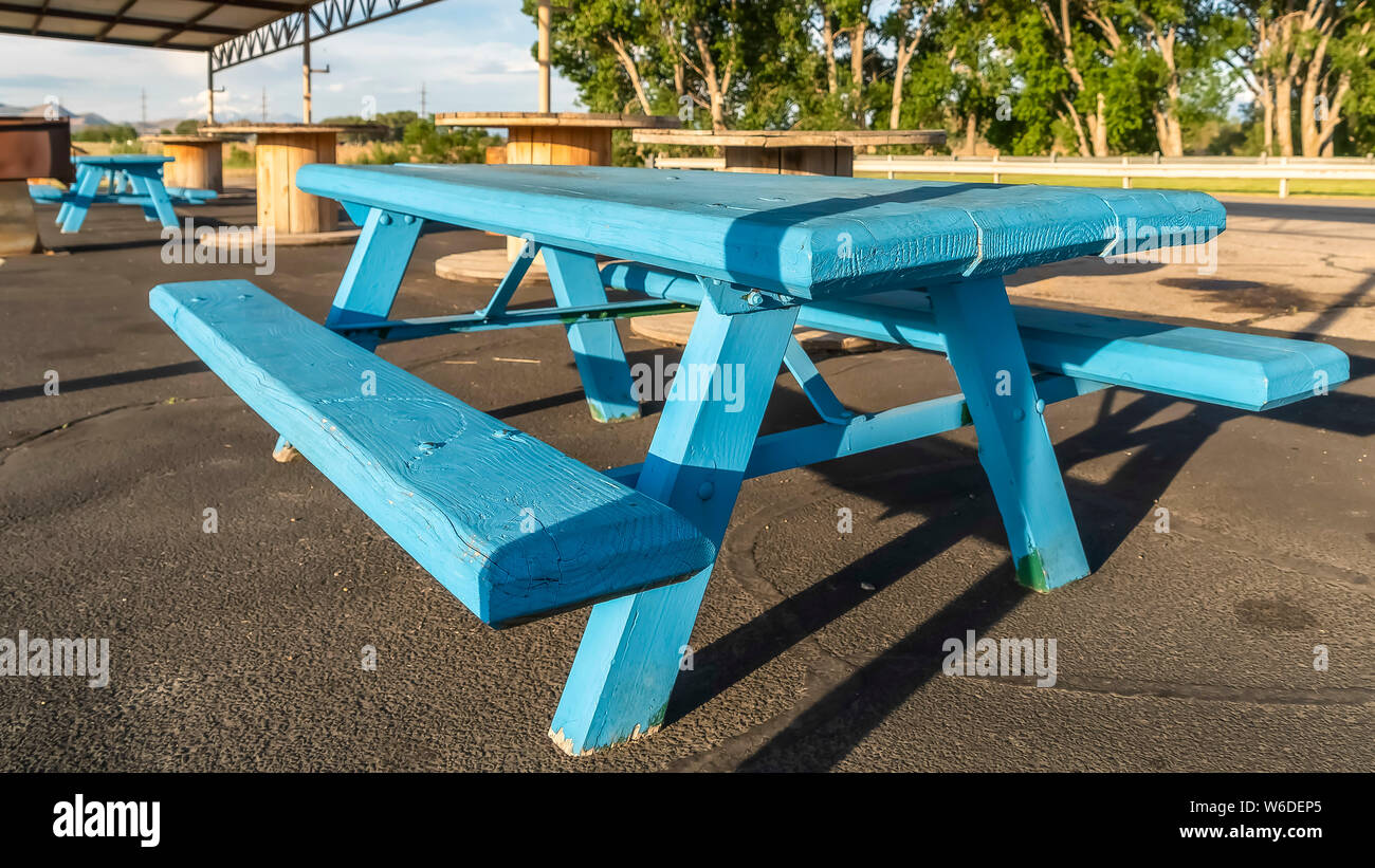 Blue picnic tables with seats and spool tables under a pavilion on a ...