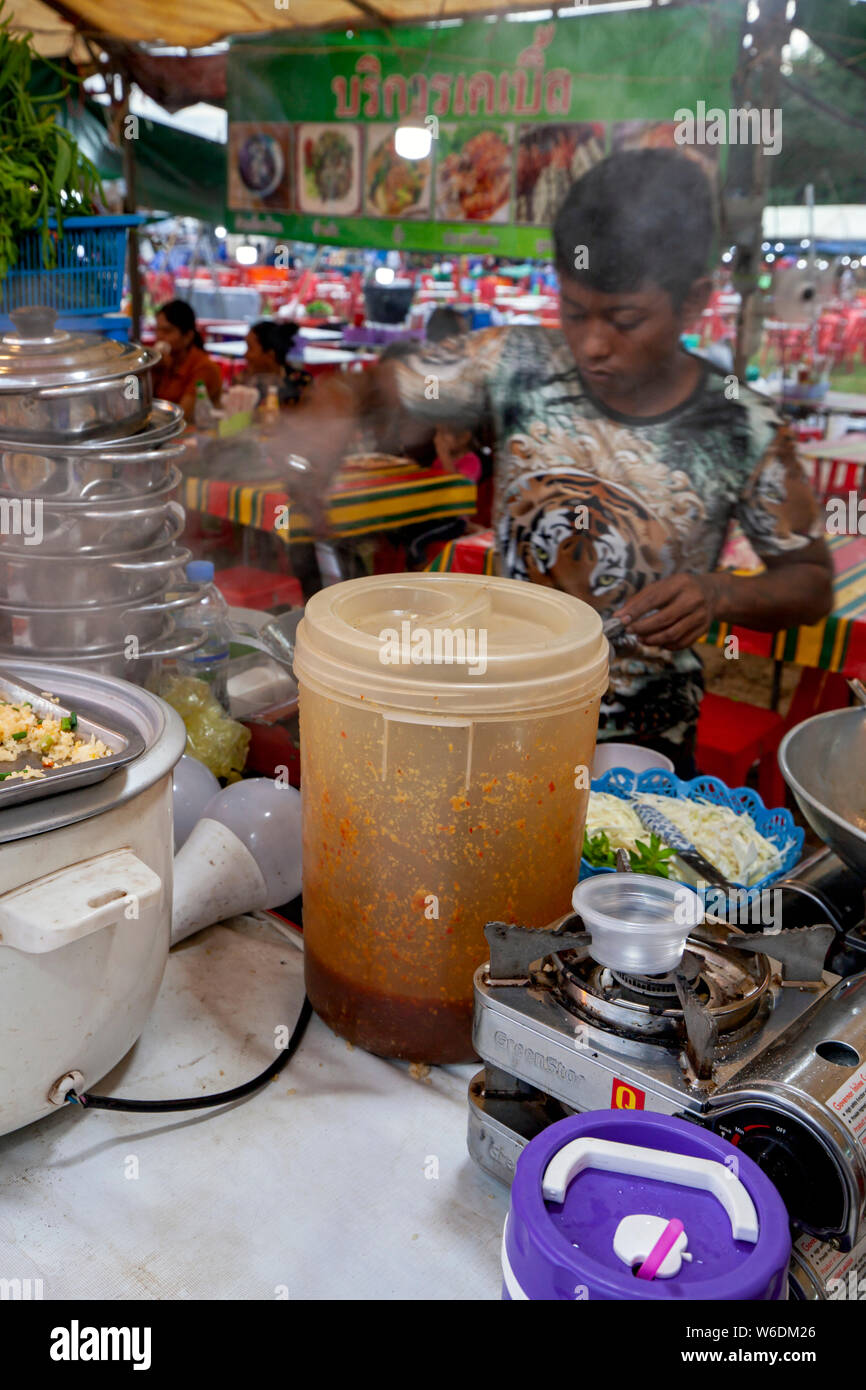 A young Cambodian man is frying brown rice in a wok at a trade fair in ...