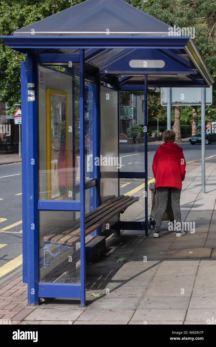 An elderly standing alone in a bus stop waiting for a bus to arrive ...