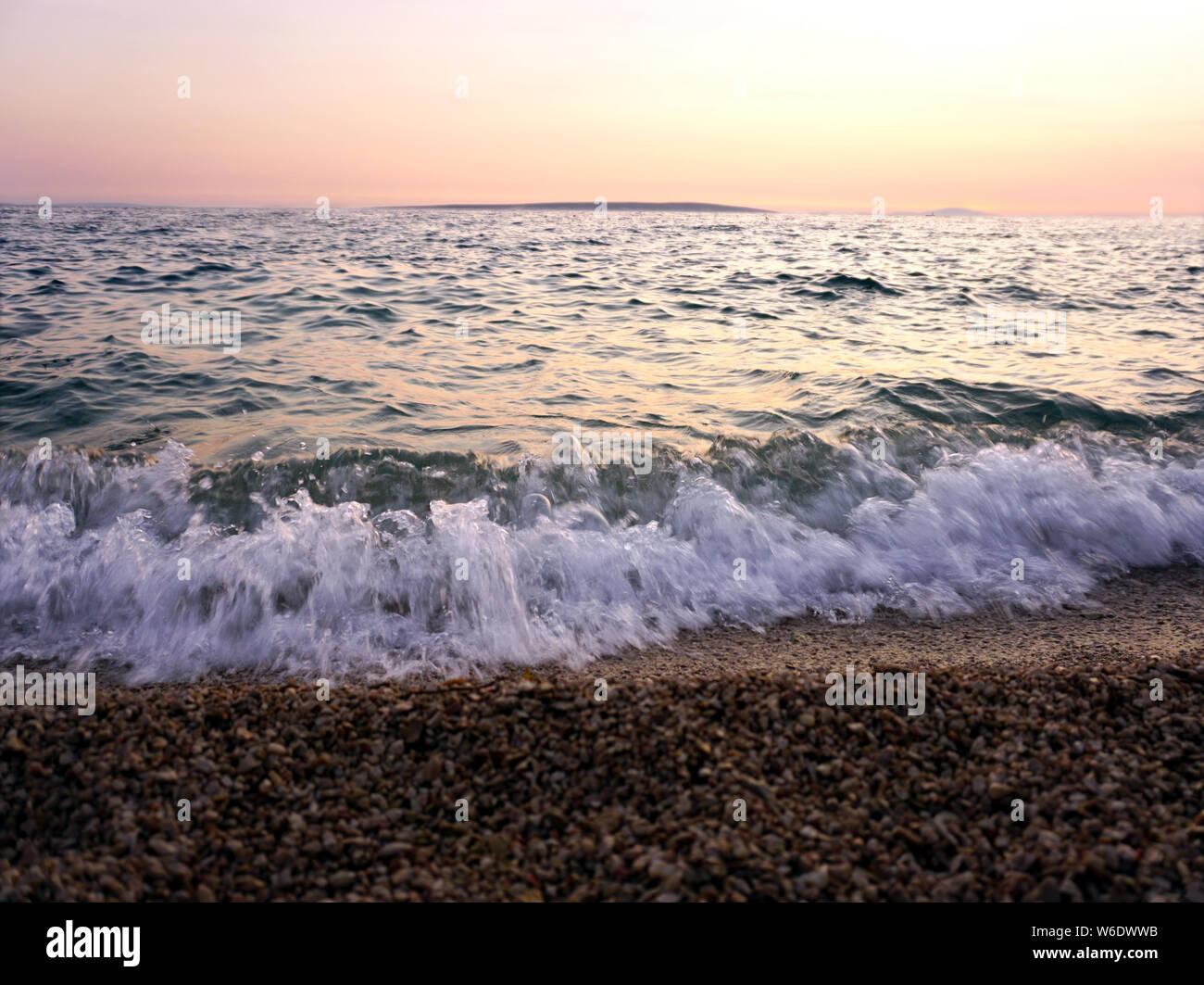 Tidal waves and sea foam on the seashore and pebble beach at sunset on ...