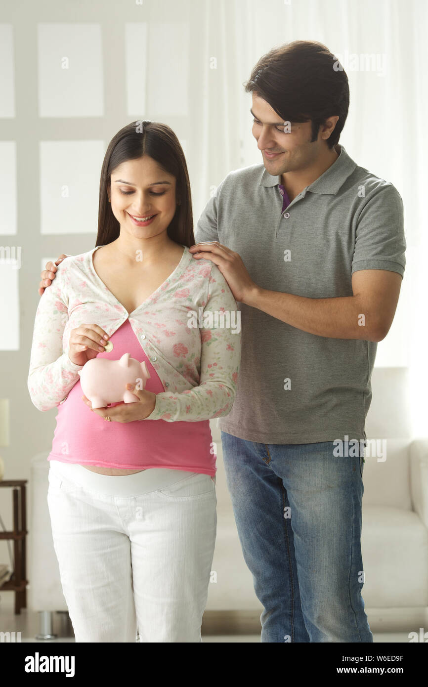 Pregnant woman putting a coin into a piggy bank with her husband Stock ...