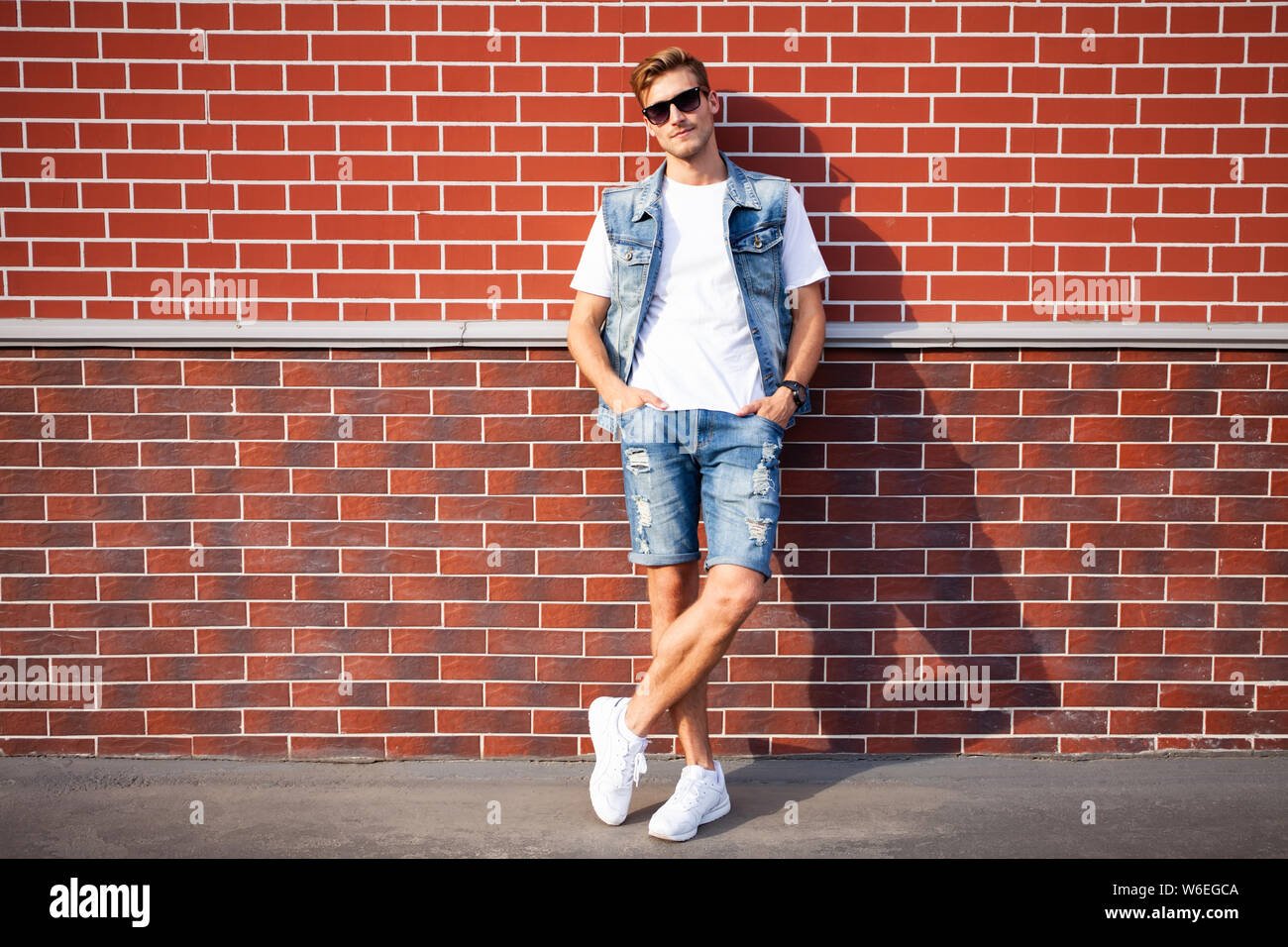 casual young man stands with his back against a brick wall Stock Photo ...