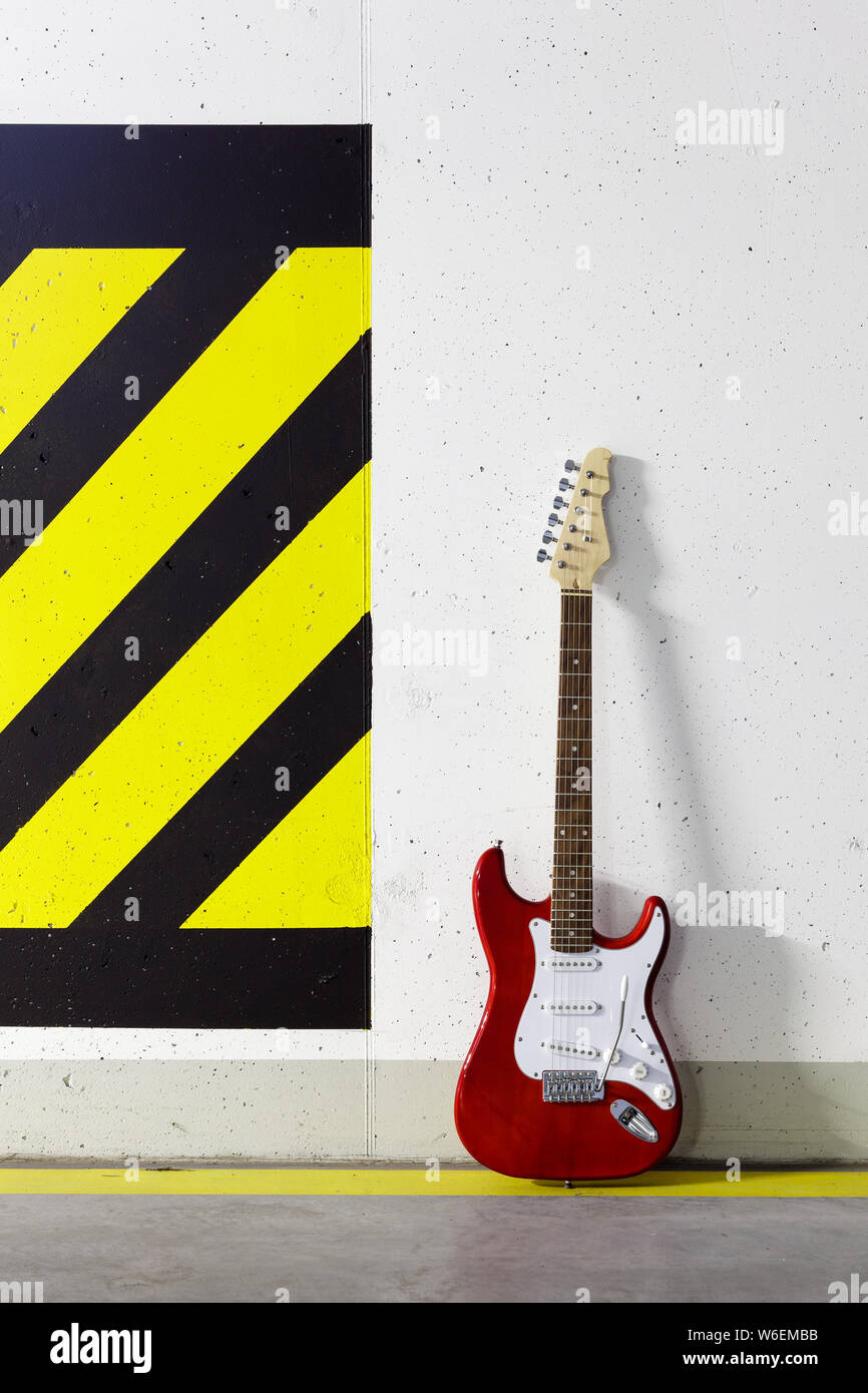 Red electric guitar stands against white raw wall, to the right of ...