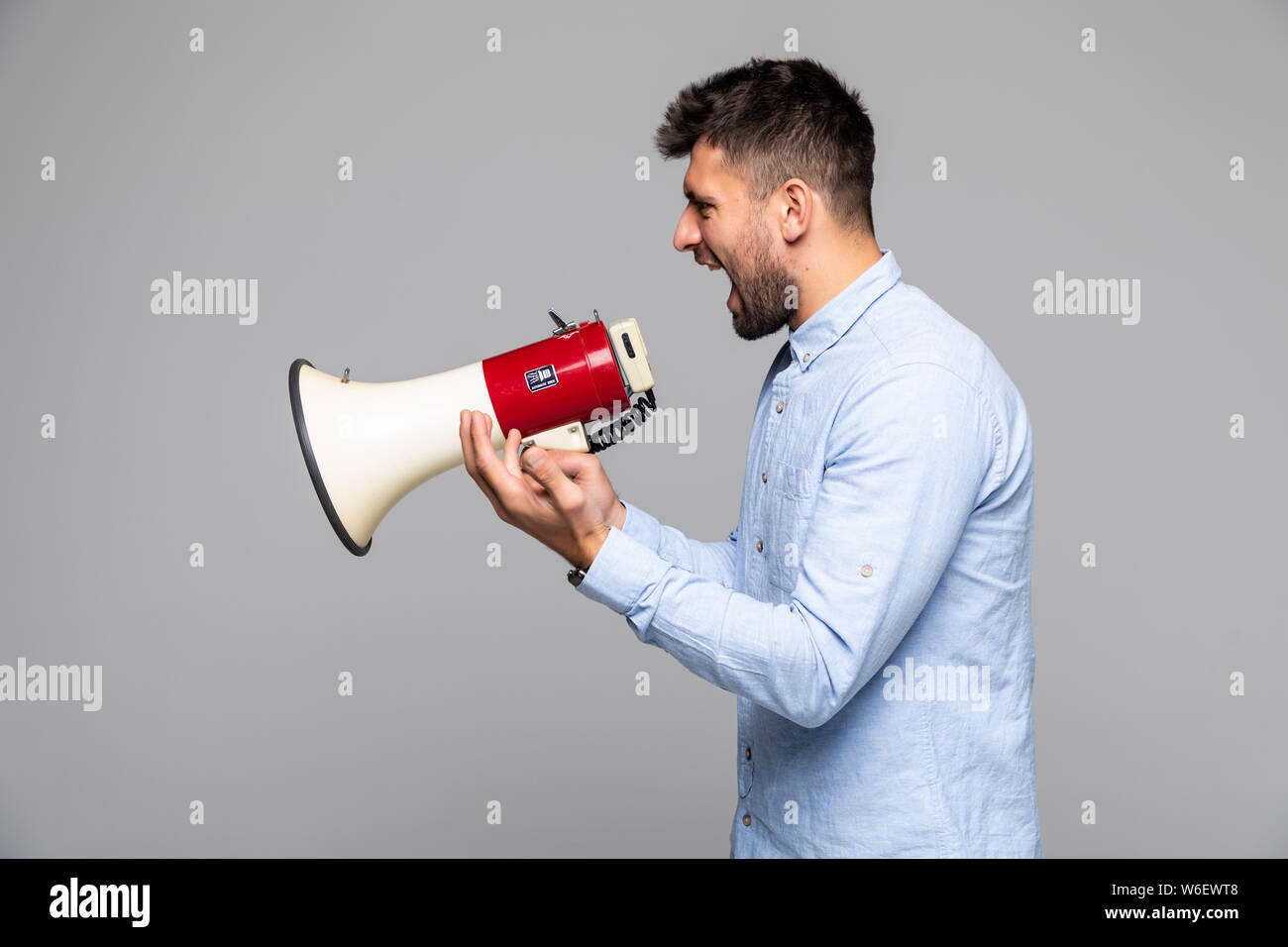 Side view of angry man shouting through megaphone against white ...
