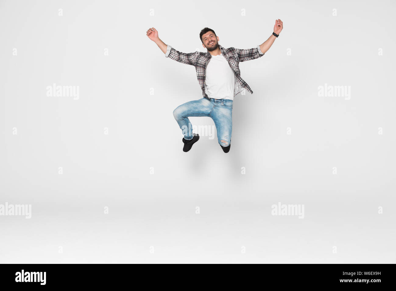 Vertical image of happy man in shirt and jeans which jumping in studio ...