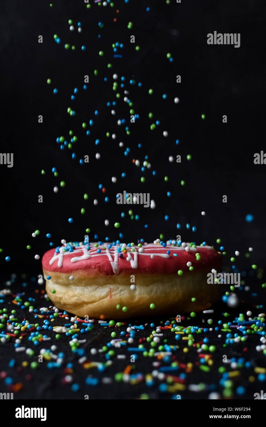 Sprinkles falling onto donut on black background Stock Photo - Alamy